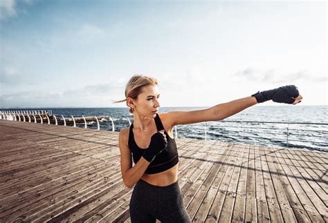 붕대에 싸인 손을 가진 젊은 여성 킥복서가 일출 에 해변에서 펀치를 훈련합니다 아침 훈련 전투기 강사에 대한 스톡 사진 및 기타