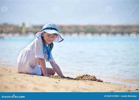 Happy Hild Girl In Big Hat And White Dress Playing Alone With Wet Sand