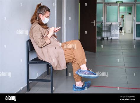 A Woman In A Face Mask Looks At The Phone In The Corridor Of The Clinic