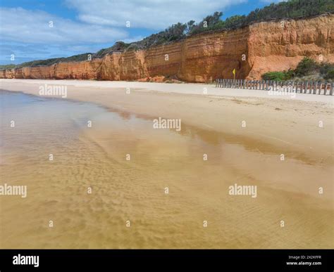 Low Angled View Of Shallow Waves On A Sandy Beach Below High Sea Cliffs