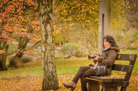 Premium Photo Mature Woman Holding Camera Sitting On Bench In Forest