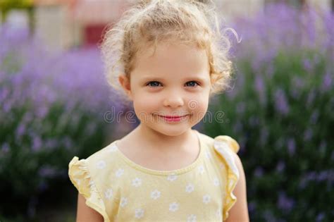 A Sweet Young Girl With Curly Blonde Hair And Blue Eyes Wearing A Yellow Dress Smiles