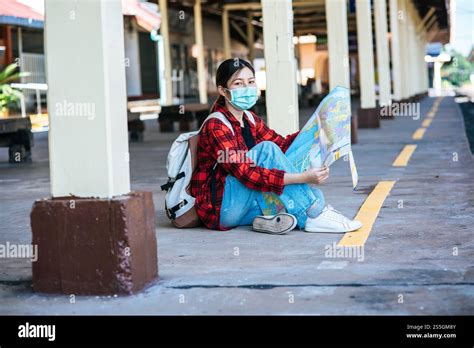 Female Tourists Sit And Look At The Map On The Footpath Beside The