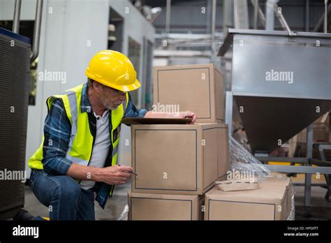 Male Factory Worker Counting Cardboard Boxes In Drinks Production
