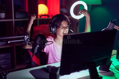 Adorable Hispanic Girl Streamer Playing Video Game With Winner Expression At Gaming Room Stock