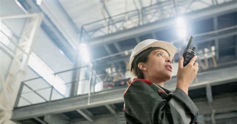 현대 공장의 대규모 작업장에 서 있는 동안 워키토키를 사용하는 보호 헬멧과 작업복을 입은 젊은 여성 엔지니어 사진 Unsplash의 사진술 이미지