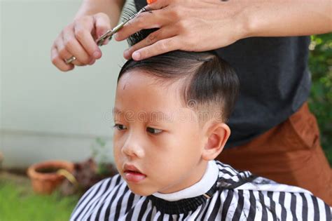 Cutting Hair Of Asian Little Boy With Barber Scissors In The Garden