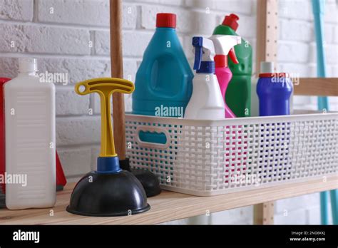Plungers And Basket With Detergents On Wooden Shelf Near White Brick