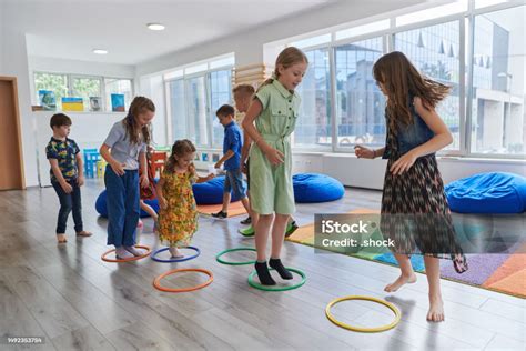 작은 보육원 아이들 교실에서 실내 바닥에 여성 교사와 함께 운동을하고 훌라 후프 서클을 뛰어 넘으면 바닥에서 추적됩니다