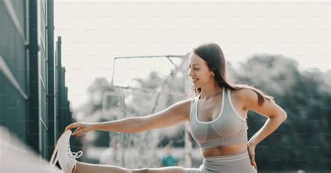 훈련에서 다리 근육 스트레칭 꽉 끼는 운동복을 입은 여성이 운동 중에 다리 근육을 스트레칭합니다 그녀는 콘크리트 울타리에 발을 올리고 거리 운동을 준비하고 있습니다