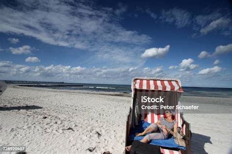 화창한 날 해변에서 두건이 달린 의자에서 휴식을 취하는 여자의 전체 길이 그늘막이 달린 비치 의자에 대한 스톡 사진 및 기타 이미지 그늘막이 달린 비치 의자 50 54