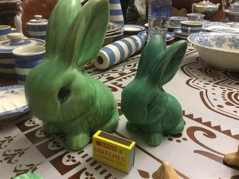 Two Green Plastic Rabbits Sitting On Top Of A Table Next To Each Other