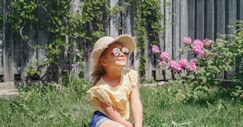 선글라스와 밀짚모자를 쓴 귀여운 사랑스러운 소녀가 야외 잔디에 앉아 있는 초상화 행복한 미소를 짓는 백인 아이는 집 뒤뜰에서 즐거운 시간을 보내고 있습니다 놀라운 즐거운