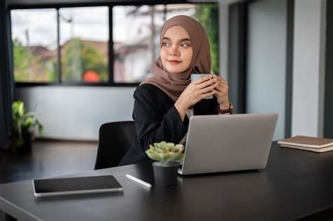 Premium Photo A Relaxed Asian Muslim Businesswoman Is Daydreaming While Having Her Morning