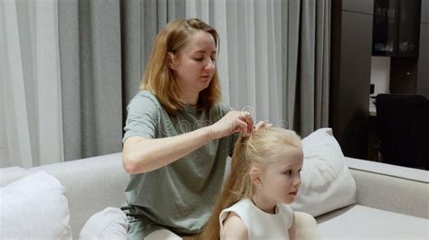 Mother Gently Braiding Daughters Hair While Sitting Together On Living