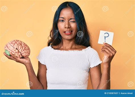 Young Indian Girl Holding Brain And Question Mark Reminder Winking