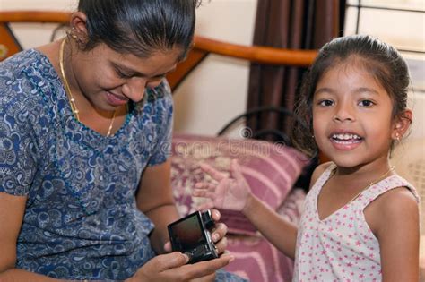 Mother And Daughter Taking Photo With Camera In Living Room At Home