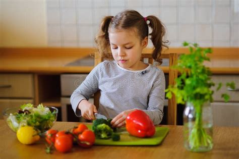 Cute Girl Of Younger School Age Cuts Vegetables And Greens For Salad
