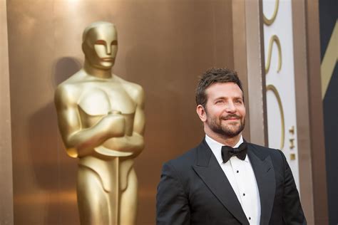 Bradley Cooper Dressed In A Tux Smiles While A Giant Golden Oscar