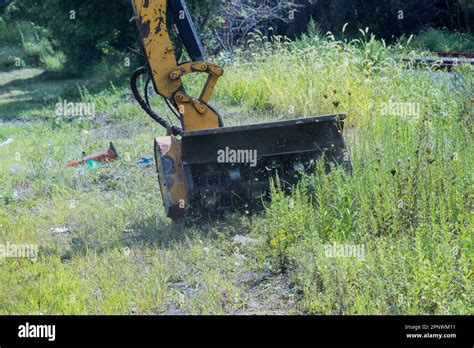 An Employee Of Utility Company Mowing Tall Grass Along Side Road Using