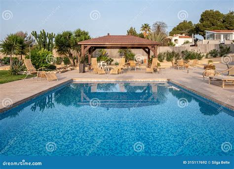 Reflective Blue Pool With A Wooden Pergola And Lounging Chairs In The