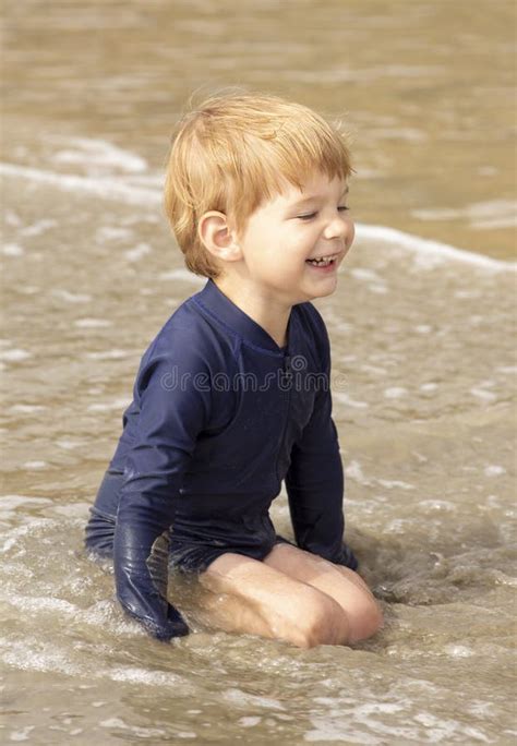 Young Boy With Blonde Hair And Navy Swimsuit Having Fun Splashing At