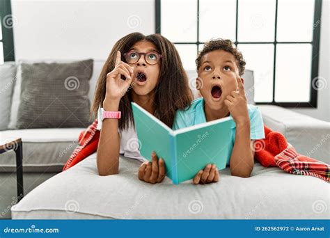 Two Siblings Lying On The Sofa Reading A Book Amazed And Surprised