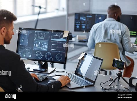 Portrait Of Male Programmer Or Data Specialist Using Computer In Office With Charts On Screen