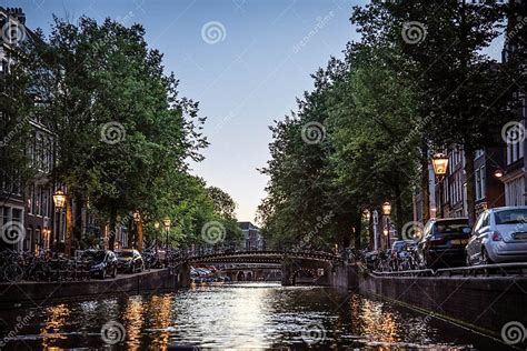 Tranquil Canal Scene With Lit Bridges At Dusk Amsterdam Netherlands