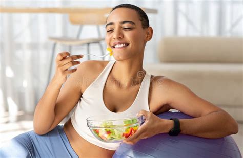 Satisfied Young Latin Woman In Sportswear Eat Salad In Kitchen Living