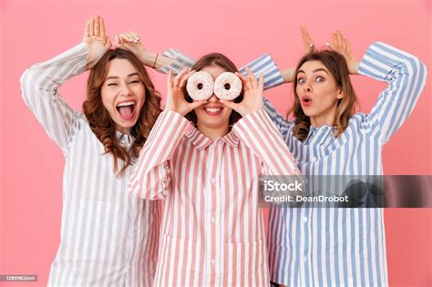 핑크 배경에 고립 된 파자마 파티에서 달콤한 디저트 도넛으로 재미있게 즐기는 여가 복을 입은 갈색 머리를 가진 20 대 여성과