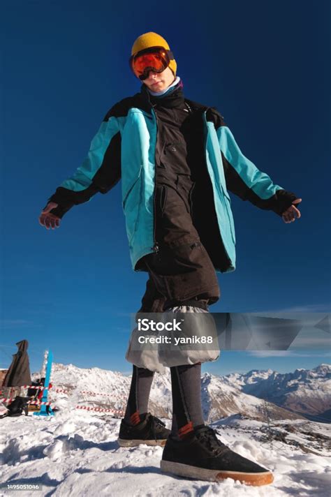 따뜻한 바람막이 모자를 쓰고 눈 덮인 산을 배경으로 서서 카메라를 바라보며 웃고 있는 매력적인 남자 추운 겨울의 개념 겨울에