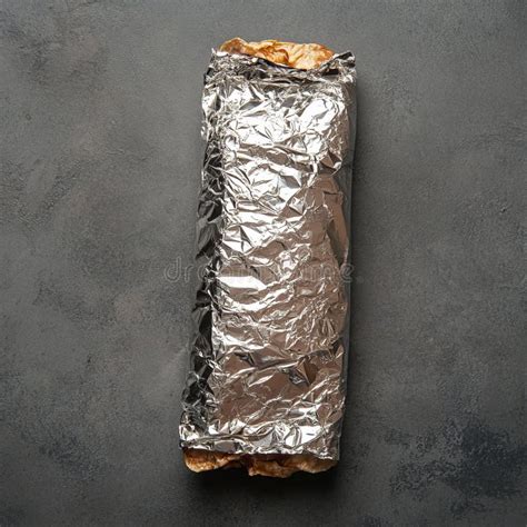 Foil Wrapped Burrito On Dark Gray Surface For Tasty Meal Stock Image