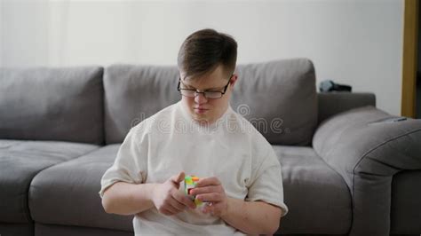 Down Syndrome Man Resting On The Couch At Home And Playing With Rubik