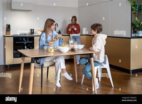 Familienfrühstück in der Küche sohn der mutter sitzt am Tisch essen Tochter telefoniert in