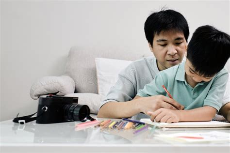 Loving Father Sits Closely With His Young Son Guiding Him As He Draws