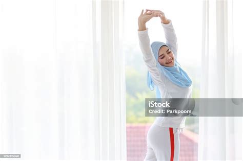 하얀 무슬림 잠옷을 입고 일출에 아침에 일어난 후 팔을 뻗는 아름다운 아시아 여성 파란 히잡을 쓴 귀여운 소녀가 행복하고 웃는 얼굴로 서서 휴식을 취하고 있다 20 24세에