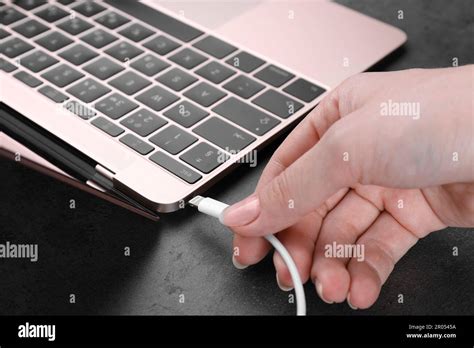 Woman Plugging USB Cable With Lightning Connector Into Laptop Port On Dark Table Closeup Stock
