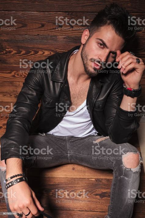 Man In Leather Jacket And Jeans Sitting On Wooden Background Stock