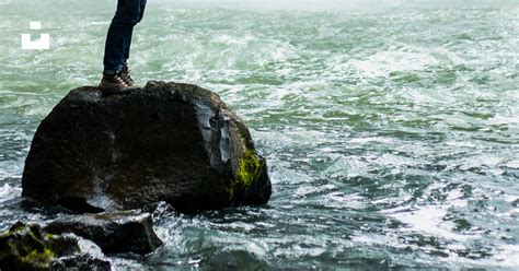 Man Standing On Black Rock Surrounded Body Of Water Photo Free