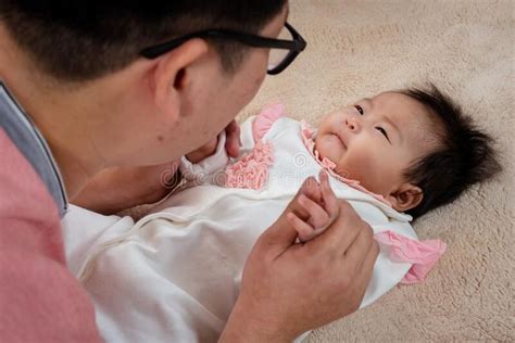 An Asian Father In Glasses Is Teasing And Playing With His 3 Month Old Newborn Daughter In Bed