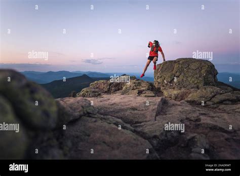 Trail Runner Man Leaping Off Rock On Top Of Mountain At Sunrise Stock