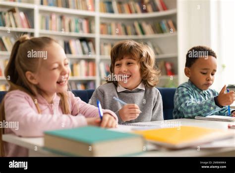 Group Of Funny Diverse International Pupils Talking And Laughing Sitting At Table With