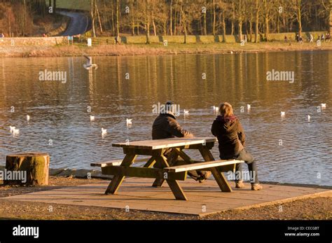 Couple Man And Woman Sitting Relaxing On Picnic Table Bench Looking