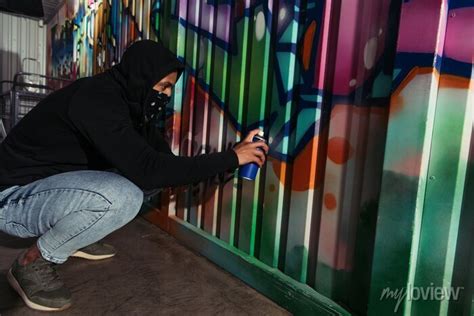 Side View Of African American Vandal In Hood Drawing Graffiti Posters