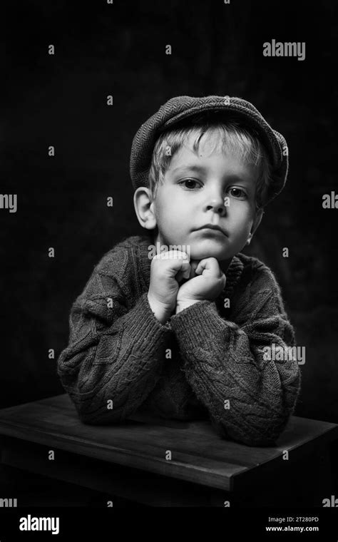 A Little Boy In A Sweater And A Retro Style Cap On A Dark Background