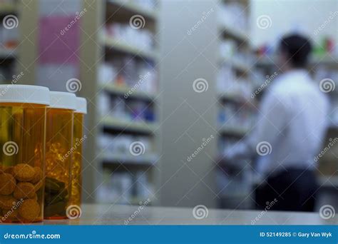 Pill Bottles On A Pharmacy Counter With Pharmacist In Background