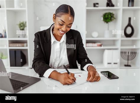 Happy Black Female Business Analyst Writing On Papers Checking Data