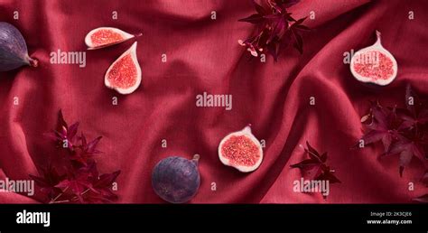 Fresh Halved Fig Fruits And Red Maple Leaves On Raspberry Red Silk