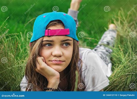 Beautiful Teen Girl With Big Eyes In A Baseball Cap Lies On The Grass